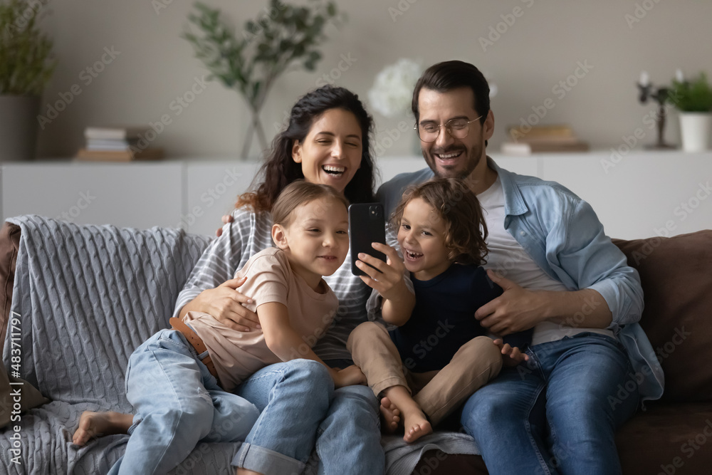 Happy couple with little kids smiling looking at cell phone screen make ...