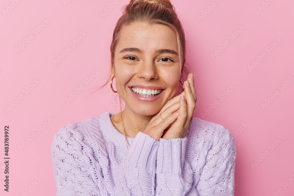 Portrait of lovely young woman smiles toothily keeps hands near face ...