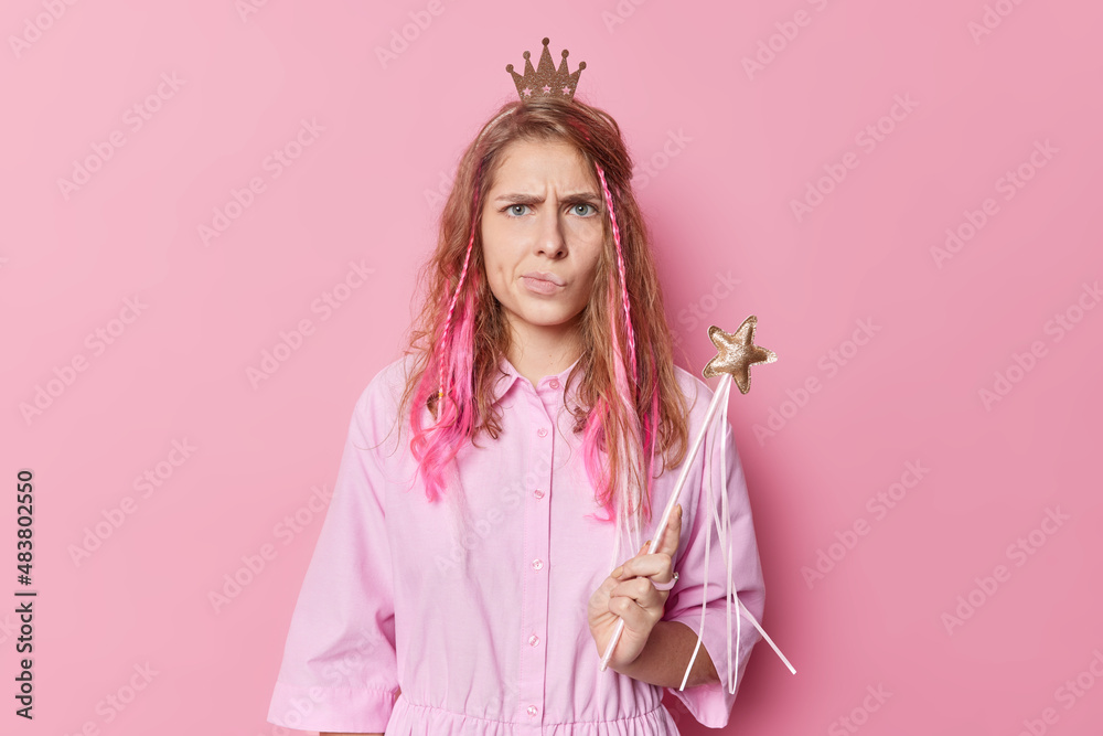 Discontent angry young woman with long hair looks gloomy wears crown ...