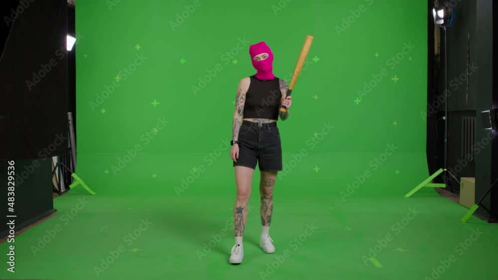 Young woman in pink balaclava with baseball bat in hands. Hooligan girl ...