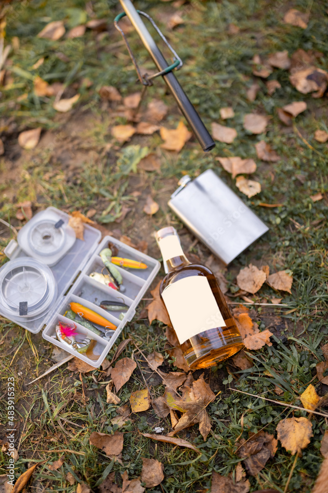 Bottles with alcohol drinks lying on the grass with fishing tackle ...