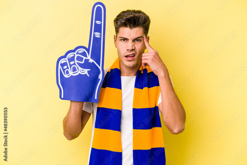 Young sports fan man isolated on yellow background showing a ...