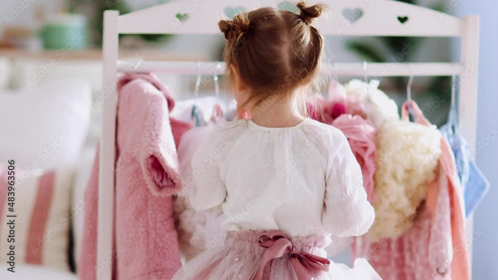 rear view of cute little girl, fashionista decides what to wear ...