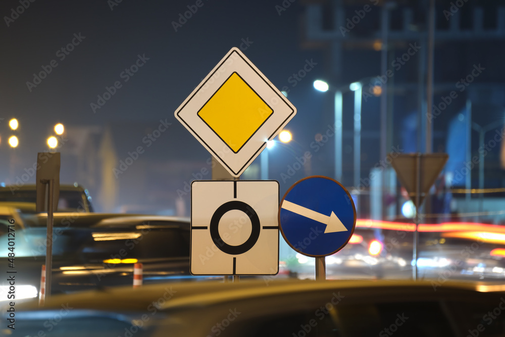 Roundabout road signs with blurred cars on city street traffic at night ...