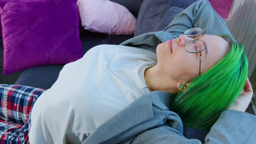 Green-haired tired, but contented girl sits on sofa, stretches, raises ...