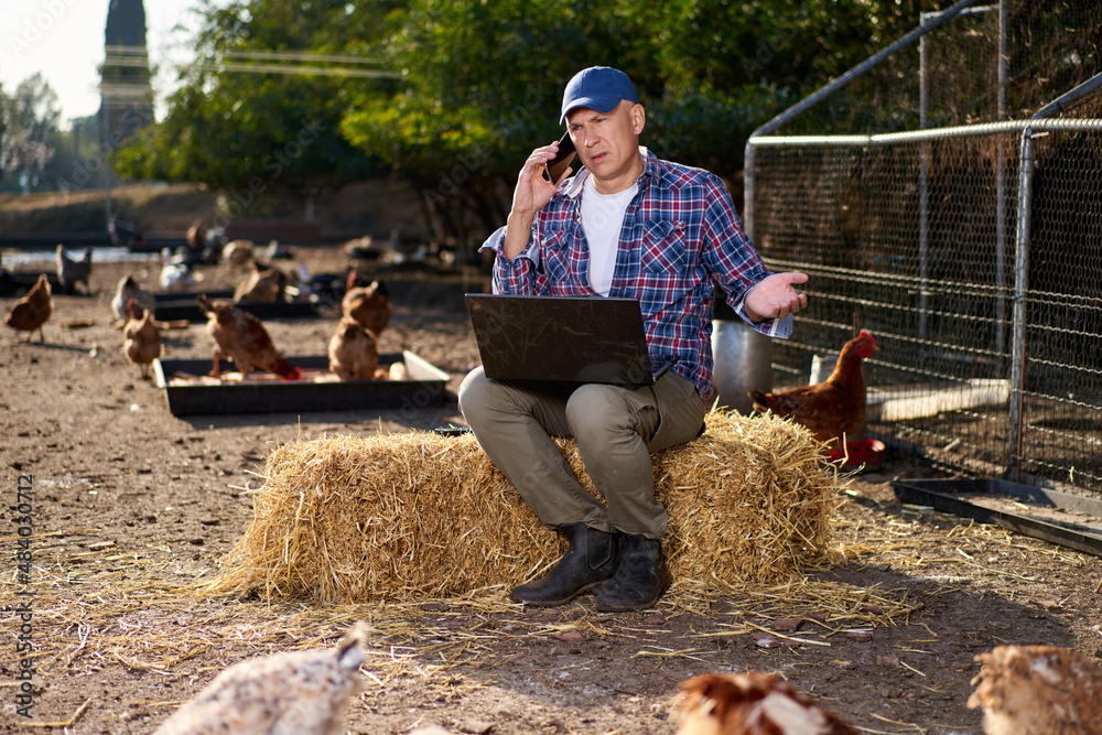 Angry man with farmer talking on the phone and hold laptop computer at ...