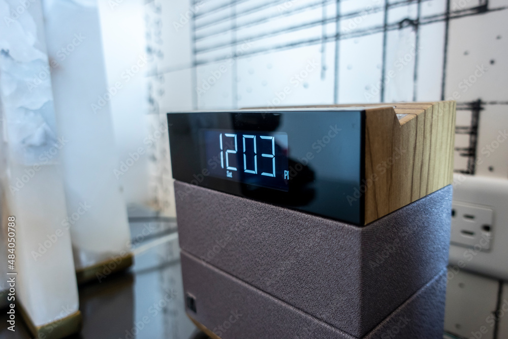 Angled view of a digital alarm clock on a bedside table in the bright ...