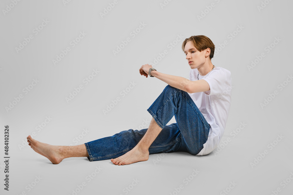 Young barefoot man sits on the floor in studio in white t-shirt and ...