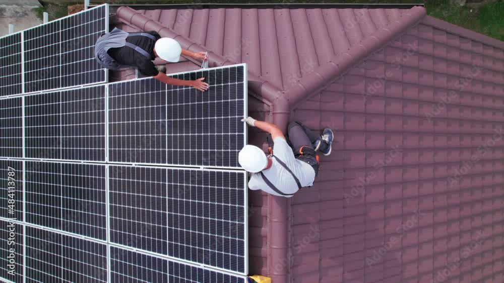 Men workers installing photovoltaic solar moduls on roof of house ...