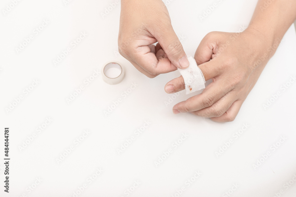 Man's finger is bandaging a gauze bandage wound from knife cut on white ...