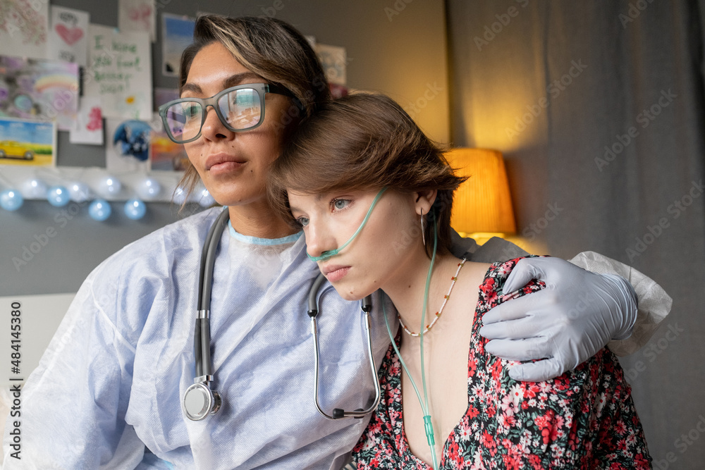 Young nurse in protective wear embracing the sad sick girl, she ...