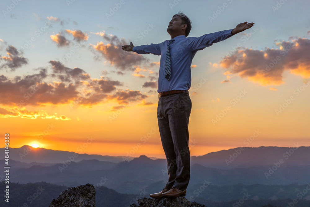Successful businessman standing raised hand on top of peak mountain ...