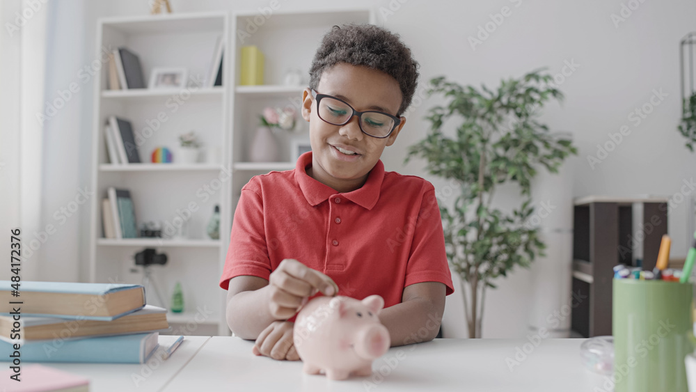 Smiling black boy putting coin in piggybank, financial literacy for ...