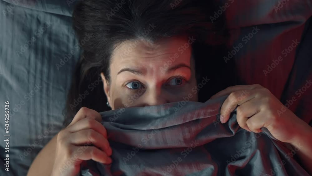 Portrait of a brunette woman in bed. She is very scared and has a ...