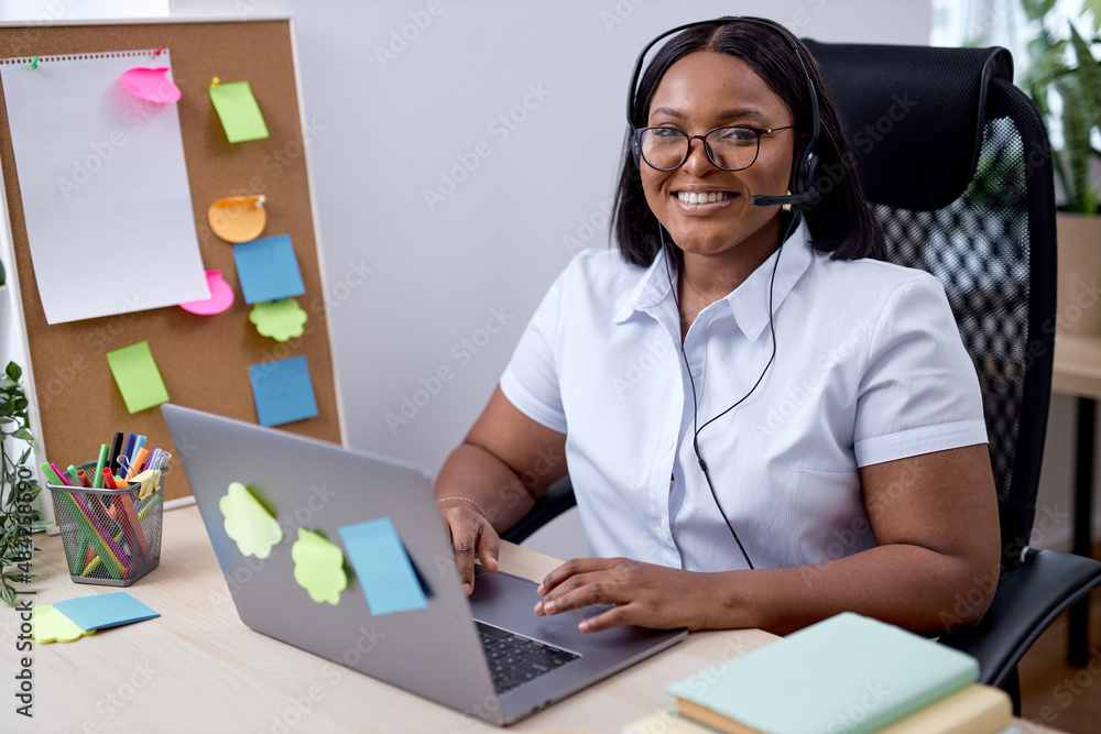 Beautiful smiling black female dispatcher with microphone working alone ...