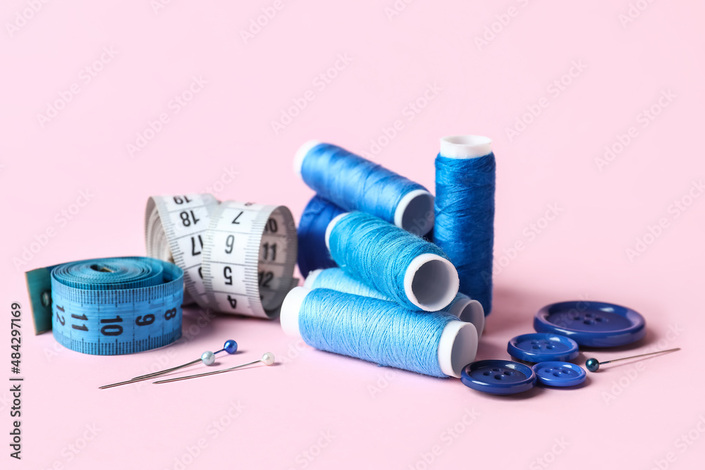 Sewing thread spools, buttons and measuring tapes on color background ...