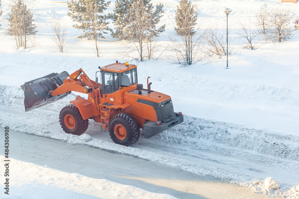 Big orange tractor cleans up snow from the road and loads it into the ...