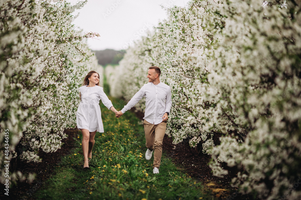 Happy family couple in spring blooming apple orchard. Young couple in ...
