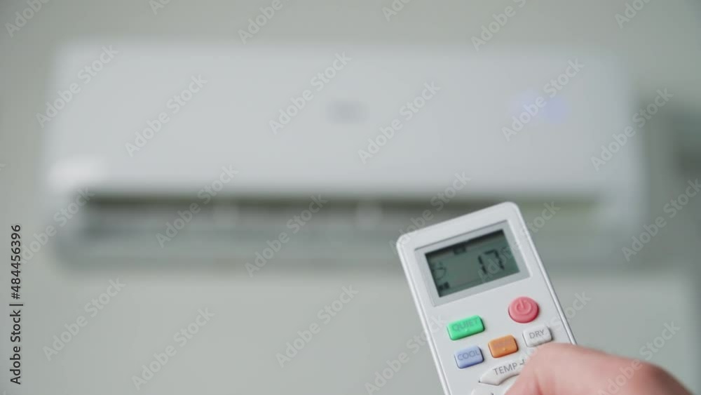 Hand adjusting temperature on air conditioner with remote control ...