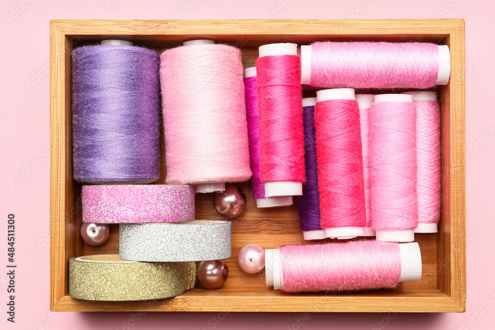 Wooden box with different sewing thread spools and tapes on color ...