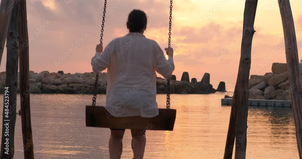 Swaying sitting on swings. A female swinging on wooden swing by the sea ...