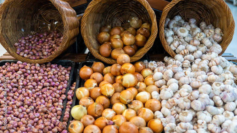 Shallots, garlic and onions on display in a supermarket basket window ...