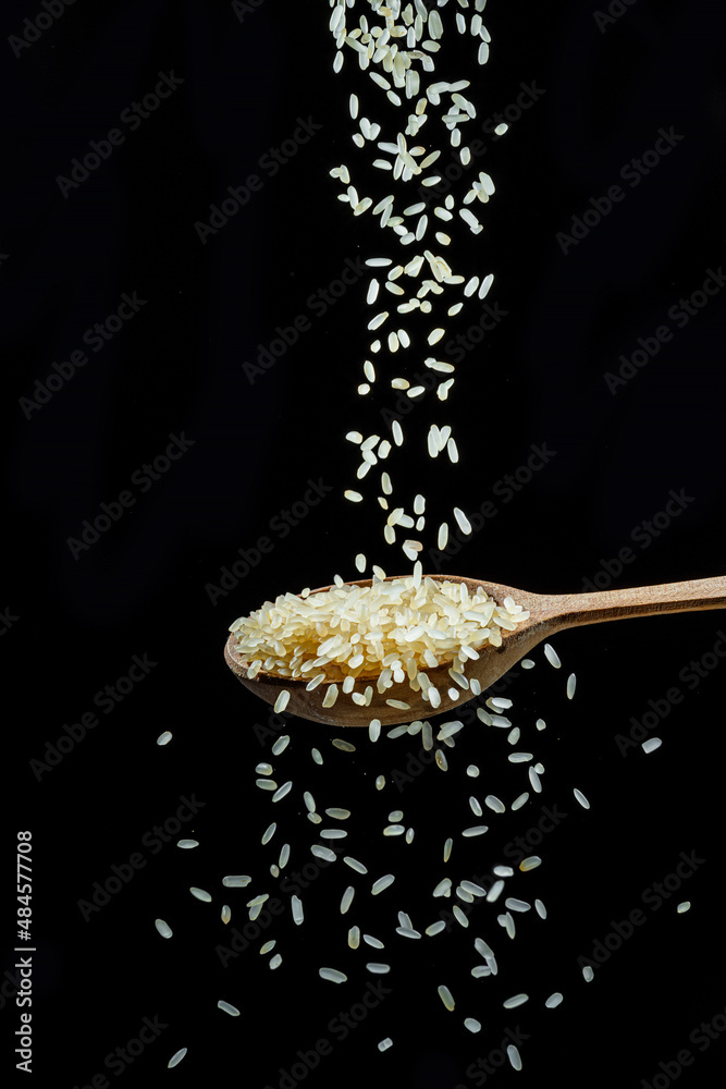 White rice grains falling down into the spoon at black background ...