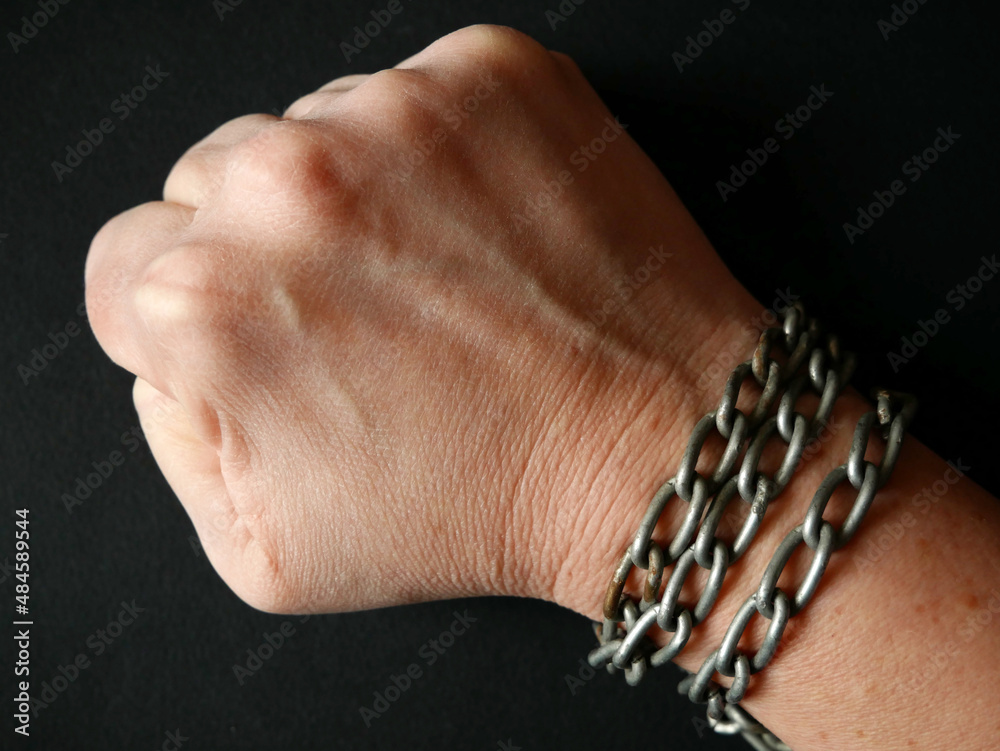 hands clenched into fists in handcuffs in the form of chains on a black ...