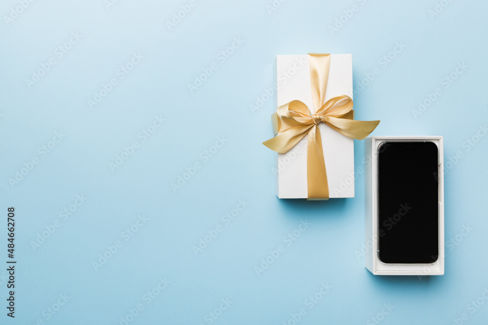Opened gift box with gold ribbon and smartphone on color background ...