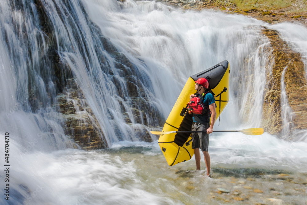 Paddler stands holding raft (packraft) below large waterfall. Stock ...