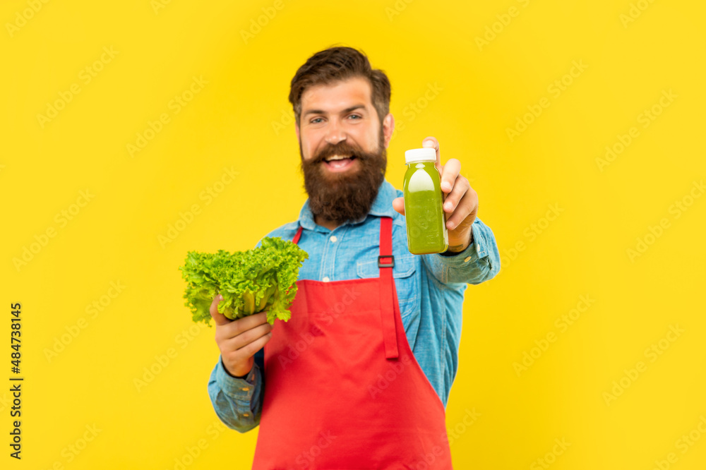 Happy man giving juice bottle holding fresh lettuce yellow background ...