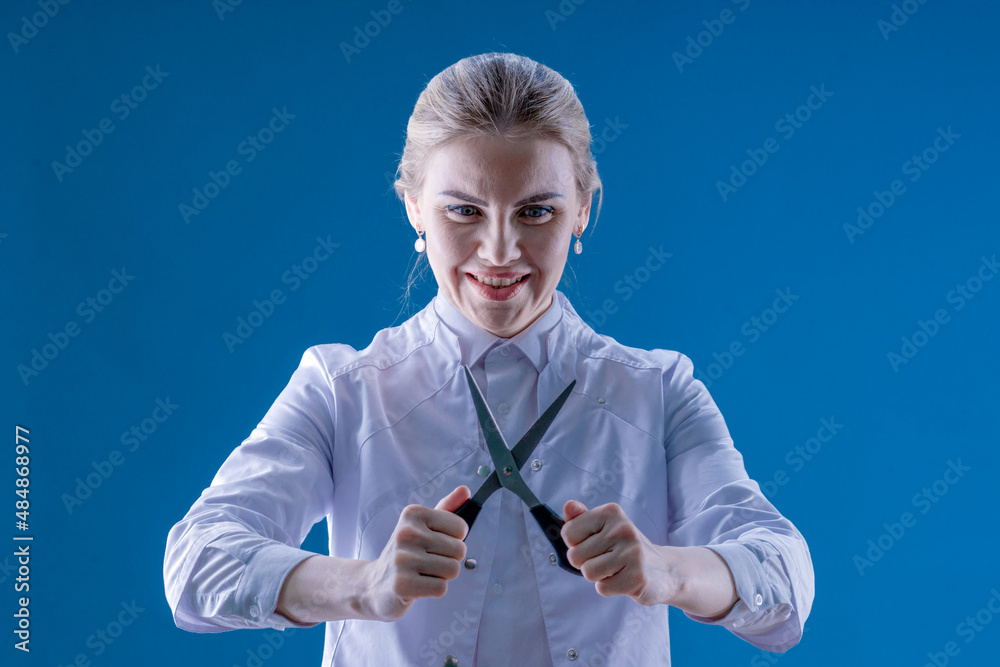 A female doctor holds scissors in her hands on a blue background ...
