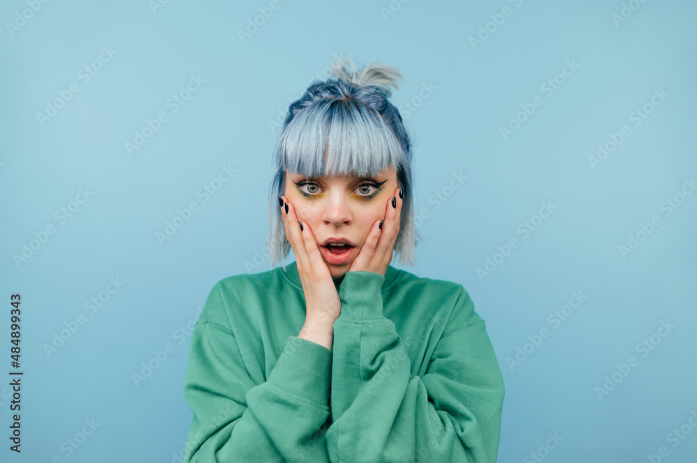 Portrait of shocked teen girl with colored hair on blue background ...