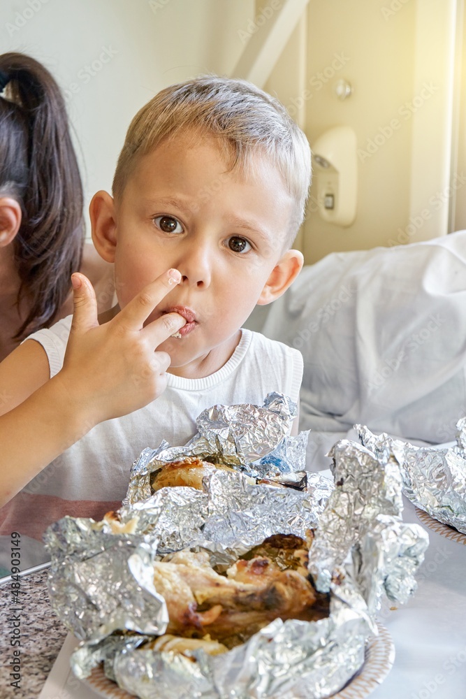 Blond little boy in mother arms licks fingers eating lunch with mouth ...