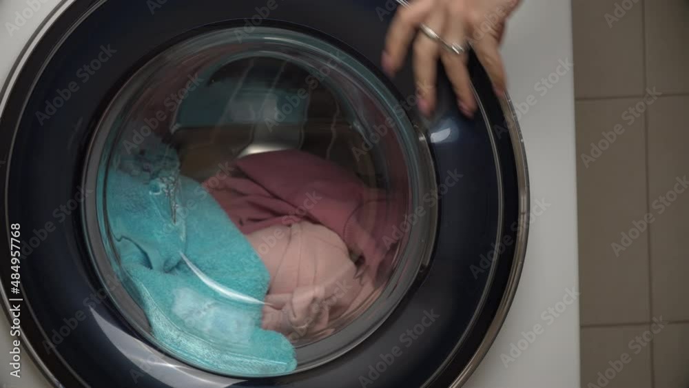 Women's hands put clothes in a modern washing machine. The girl ...