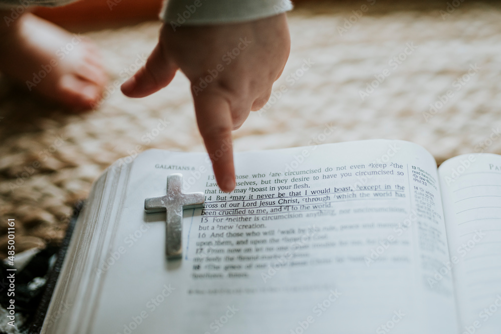 Child's hand pointing to Bible verse with metal cross on page Stock ...