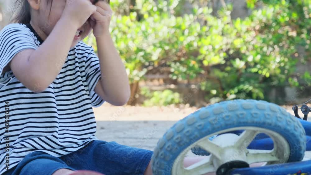 Sad little girl sitting on the ground after falling off her bike at ...