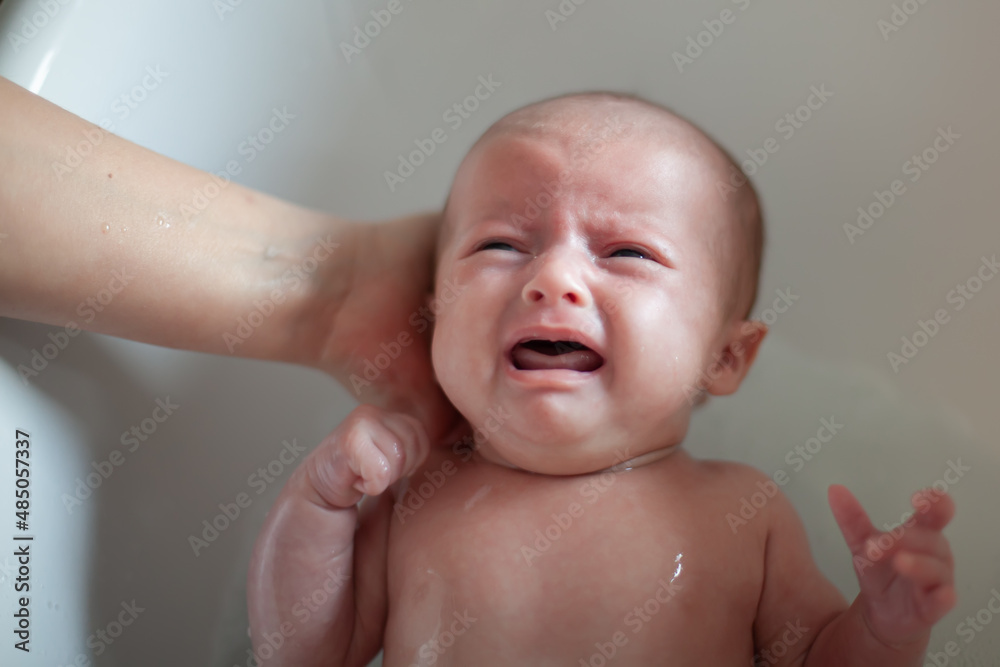Newborn baby is being bathed by his mother. Newborn baby crying in bath ...