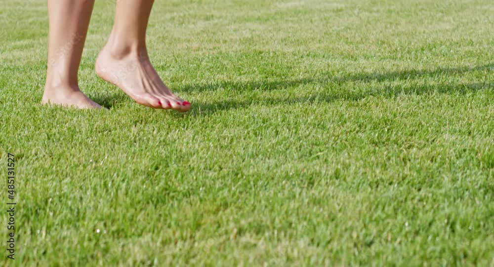 Close up of female legs with smooth skin walking on green lawn outdoors ...