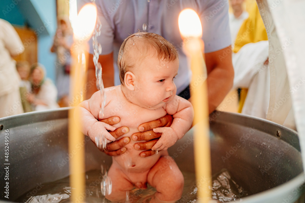 the baby boy is lowered into a font with holy water at baptism in the ...