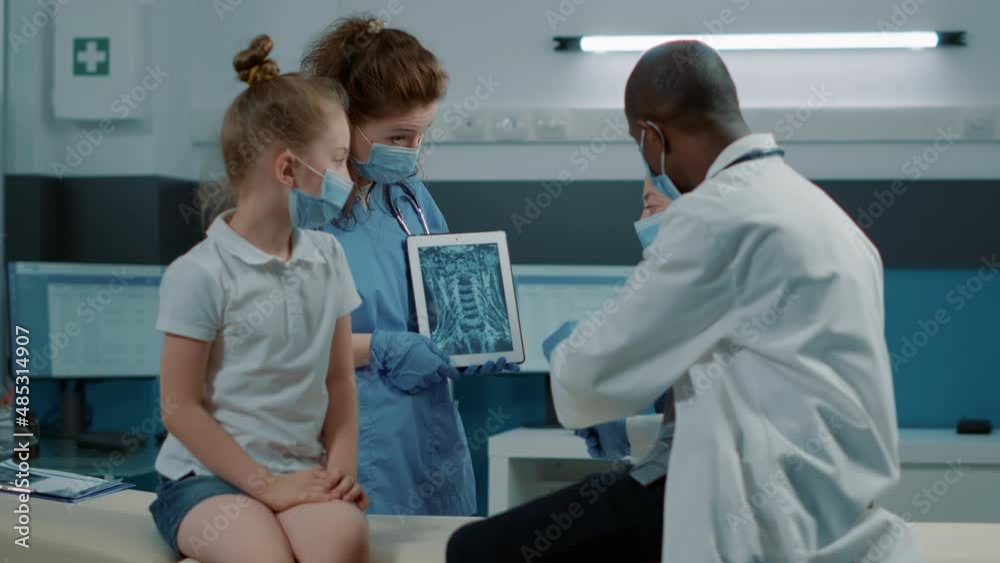 Diverse medical team explaining x ray scan diagnosis to little girl at ...