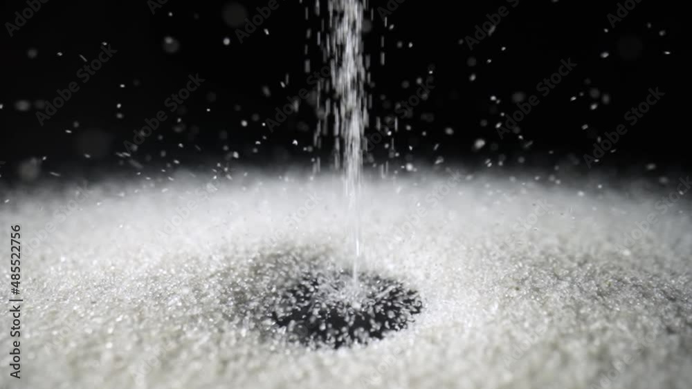 Particles of white dry sand pour in stream, hit the surface and scatter ...