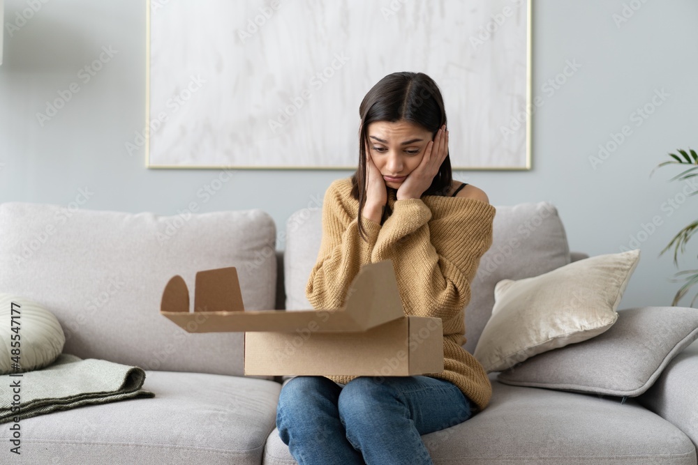 Angry confused woman unpacking parcel, wrong or broken online store ...