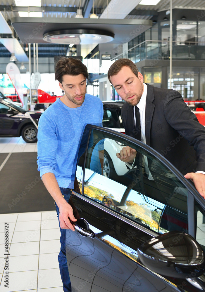 Advice in the car dealership - seller and young man selling a new car ...
