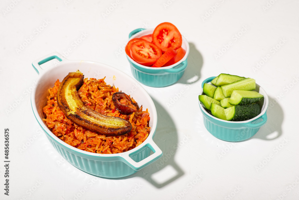 Jollof rice with fried banana. Fresh vegetables - tomato and cucumber ...