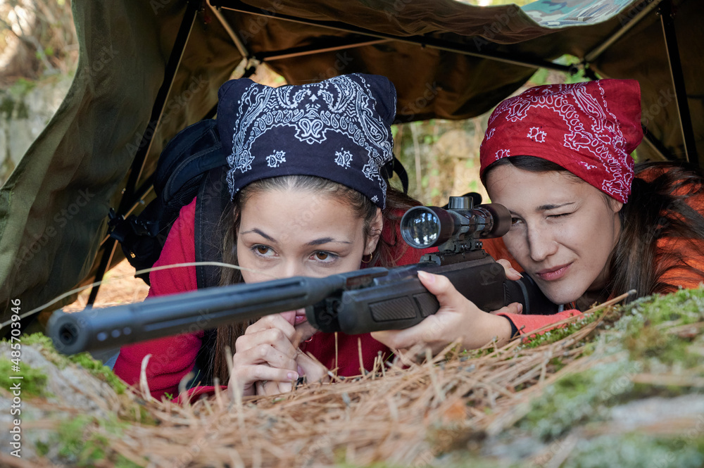 Two teenage women hunt in the woods using a shotgun hidden under a ...