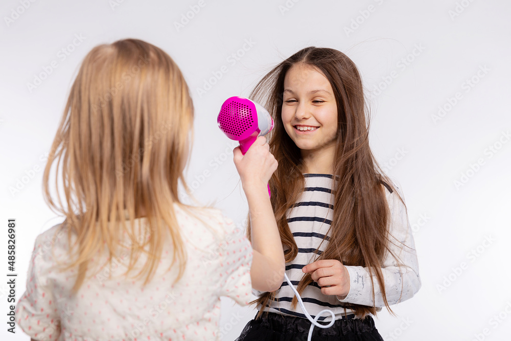Two beautiful girls 6-8 years old are playing with the hair dryer ...