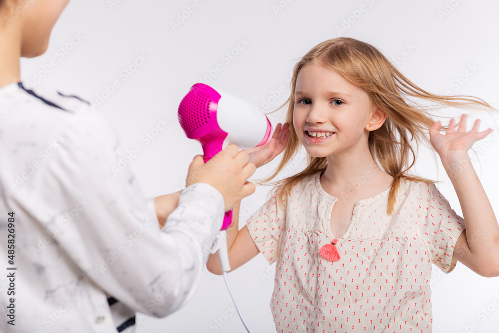 Two beautiful girls 6-8 years old are playing with the hair dryer ...