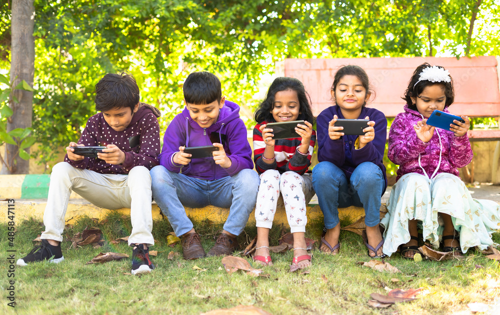 Group of kids busy using mobile phone while sitting at park - concept ...
