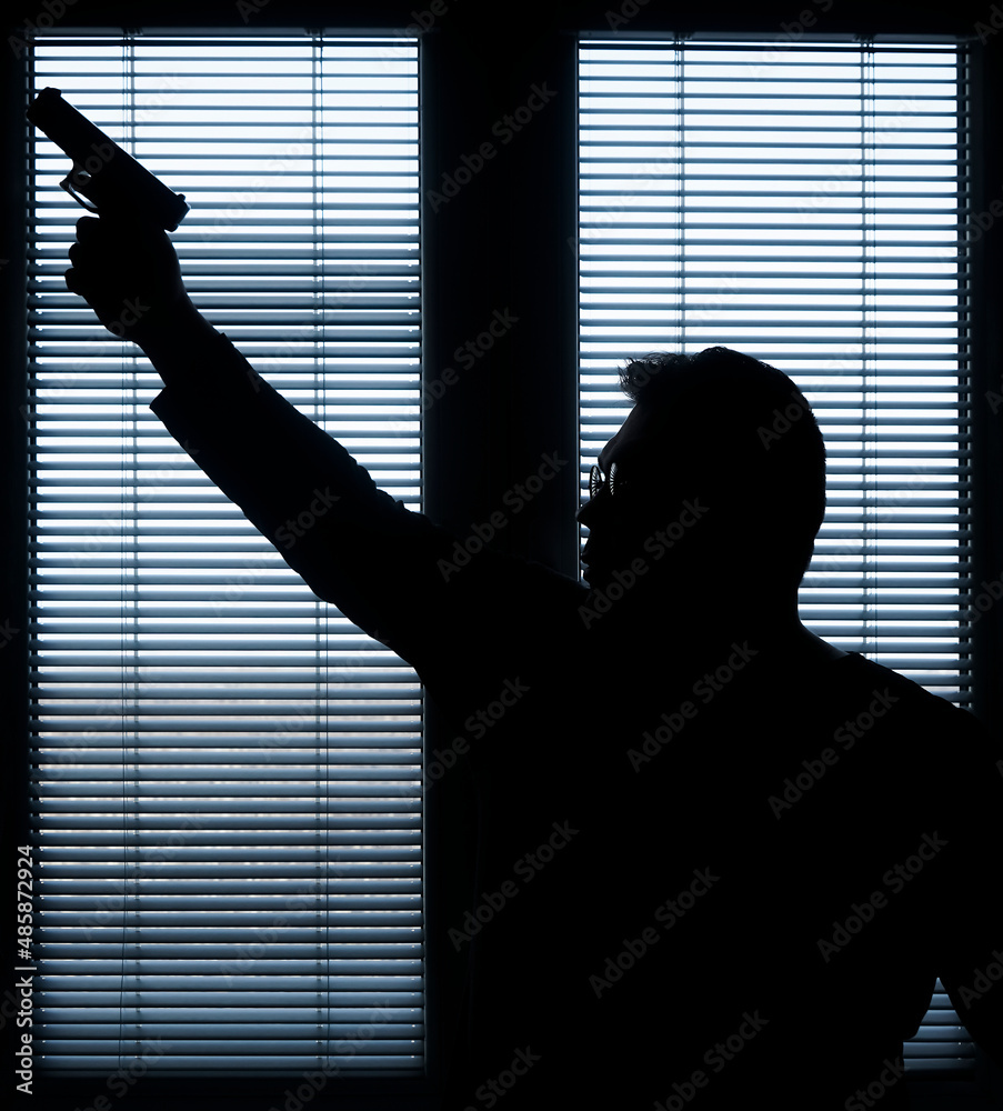 A man with a gun is standing by the window blind, ready to protect ...